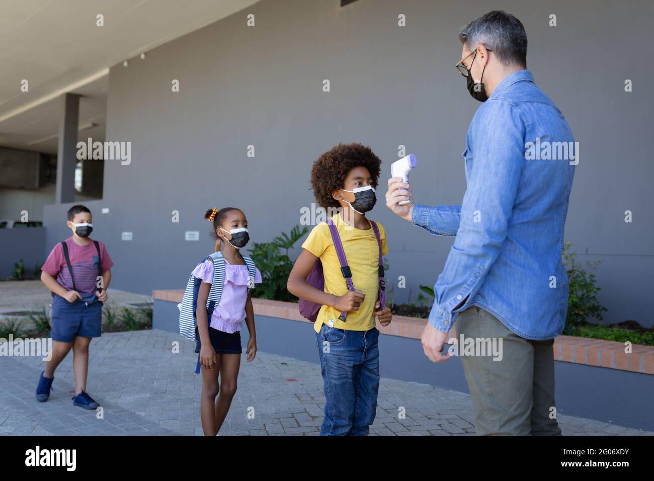Caucasian male teacher measuring temperature of students standing in a ...