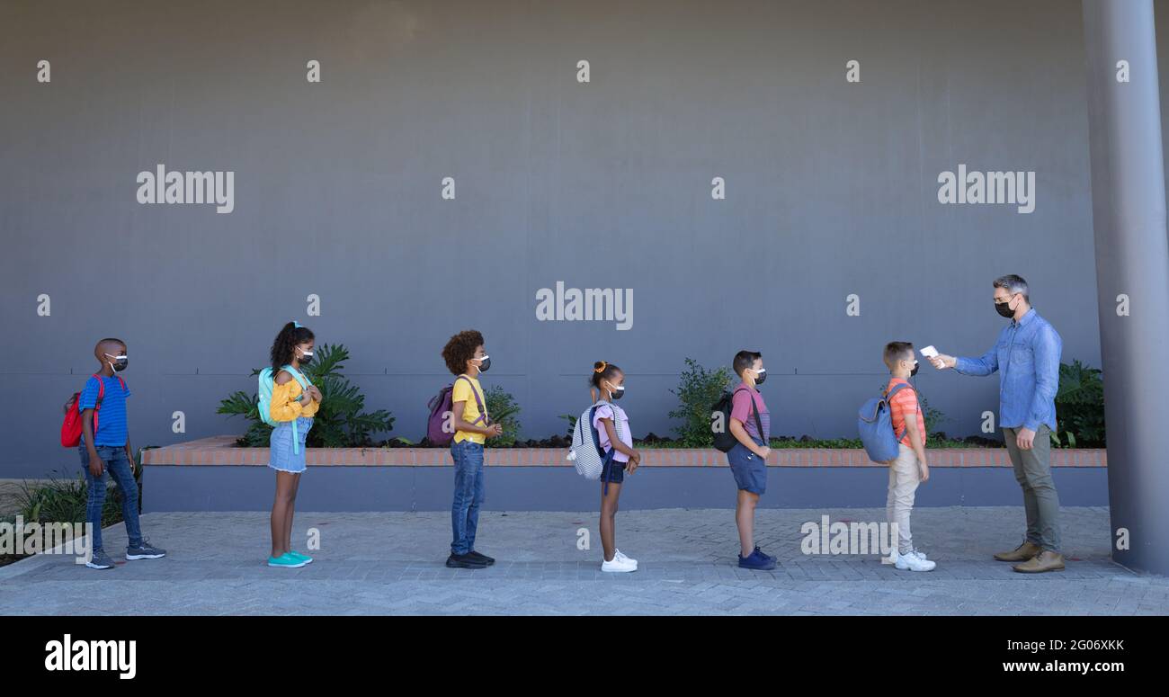Caucasian male teacher measuring temperature of group of students ...