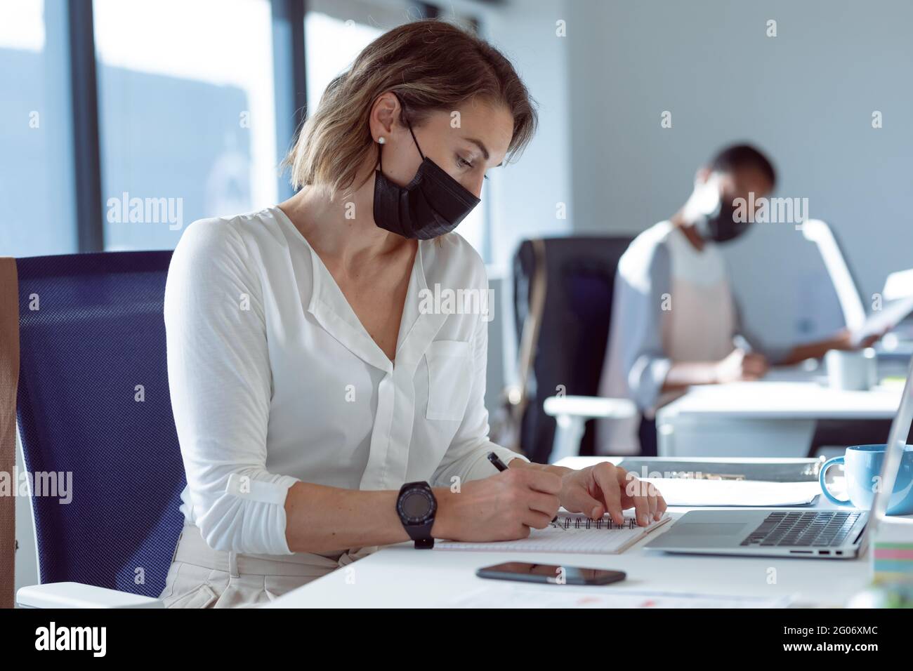 Caucasian businesswoman wearing face mask, sitting at desk, making ...