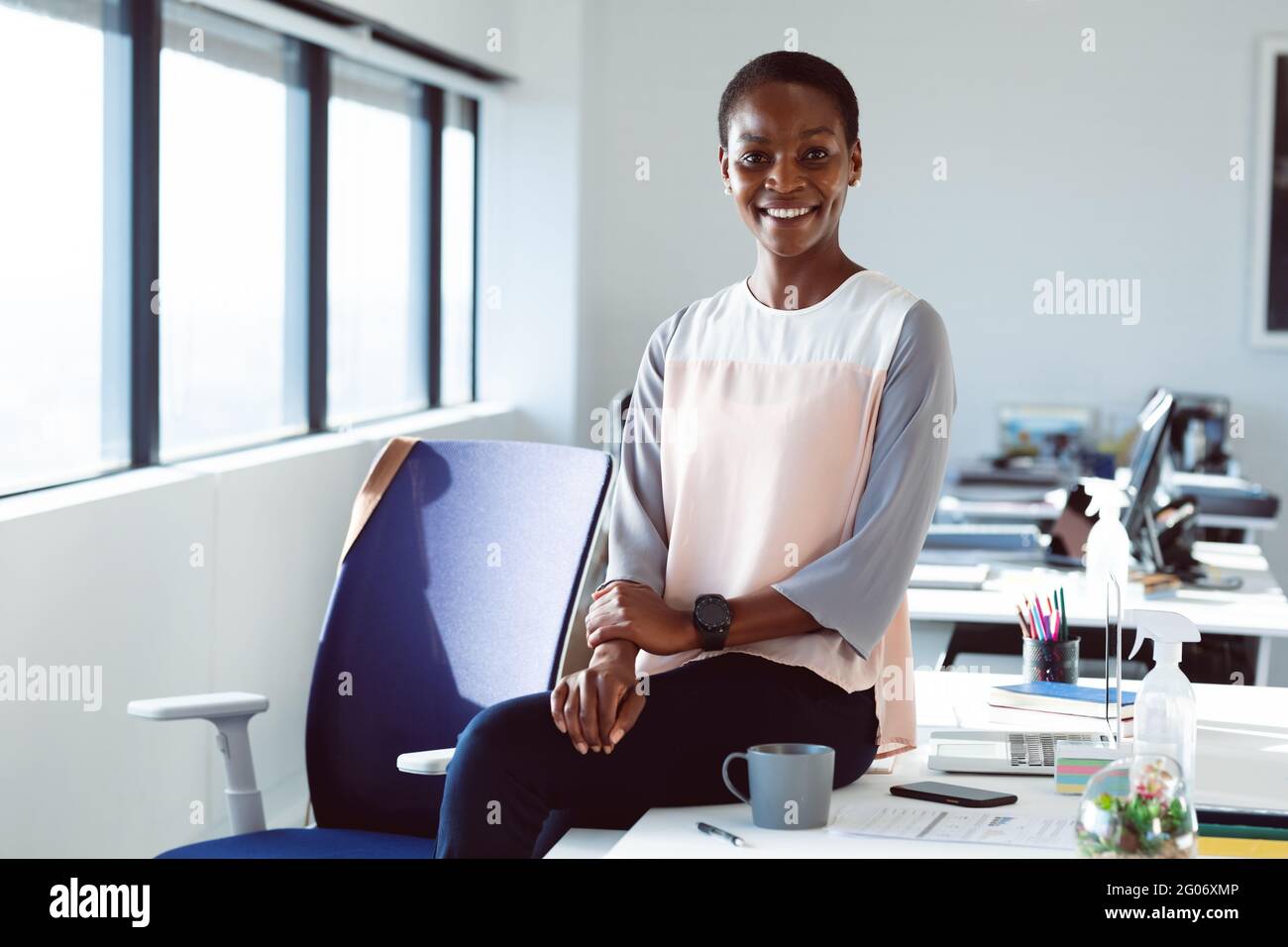 Smiling african american businesswoman sitting on desk at work Stock ...