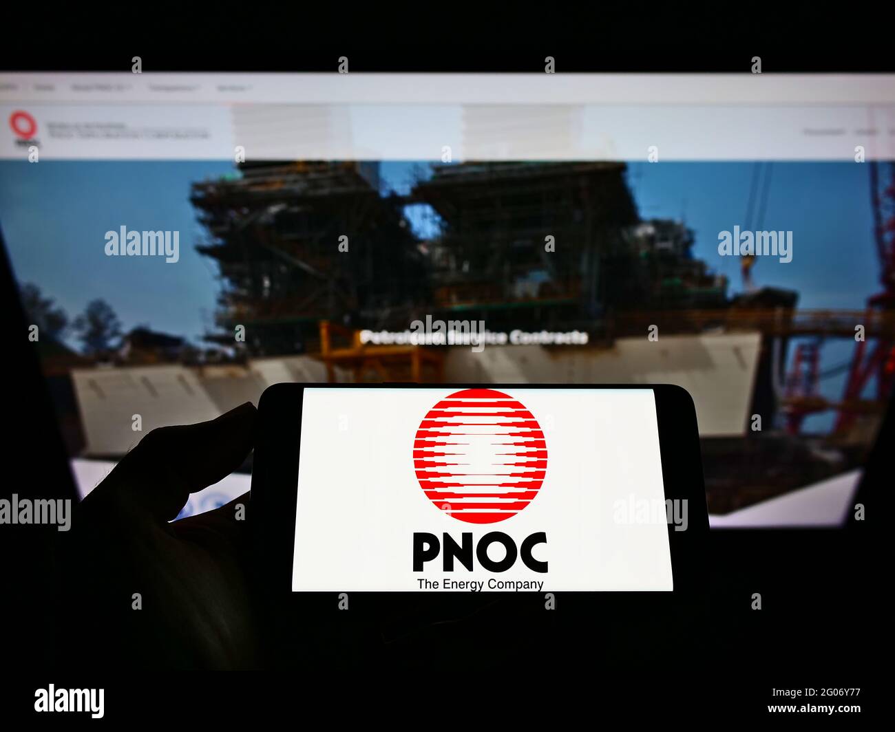 Person holding mobile phone with logo of Philippine National Oil ...