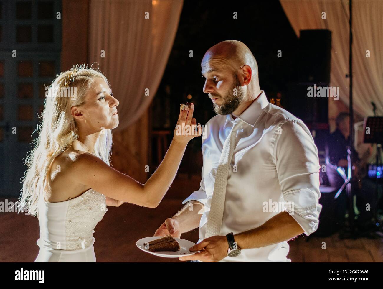 Bride and groom eating and feeding each other cake at wedding reception ...