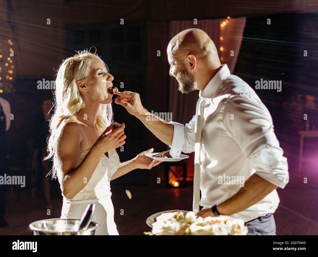 Bride and groom eating and feeding each other cake at wedding reception ...