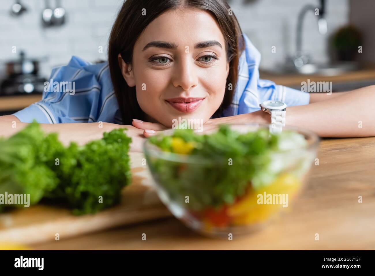 smiling young adult woman looking at prepared vegetables salad in ...