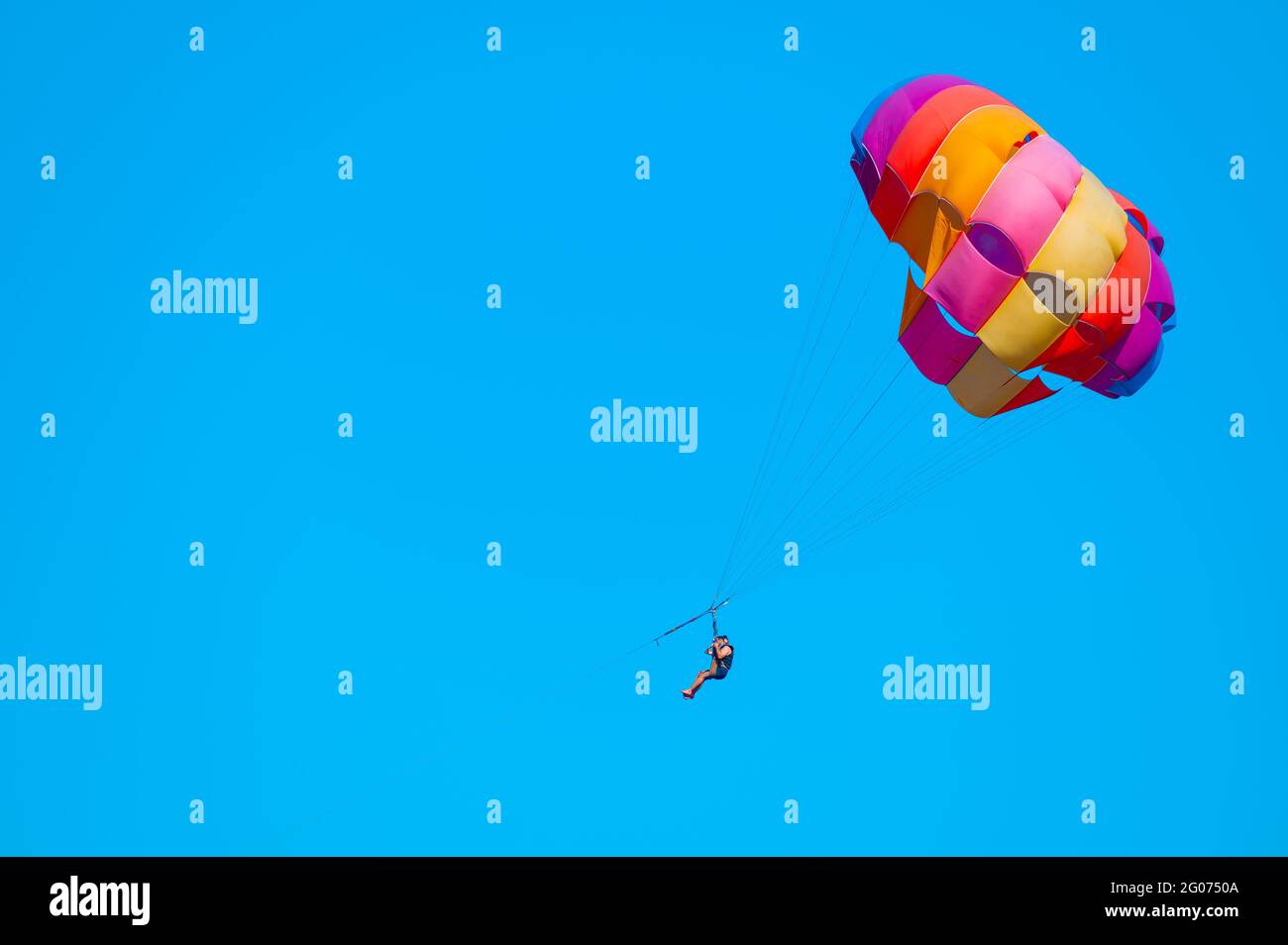 Parasailing on blue sky. Couple under parachute hanging mid air ...