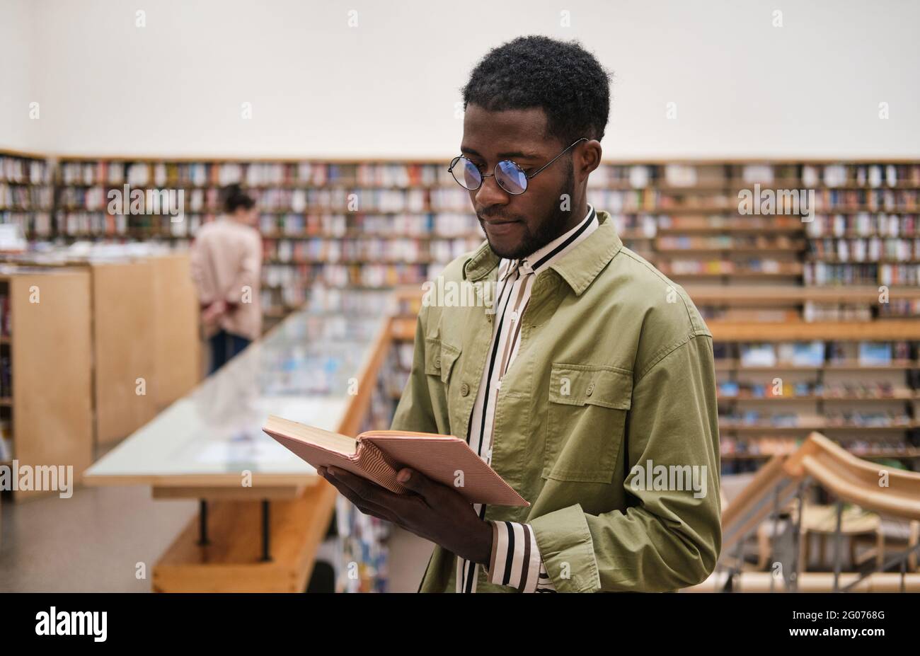 African young man in eyeglasses reading a book while standing in the ...