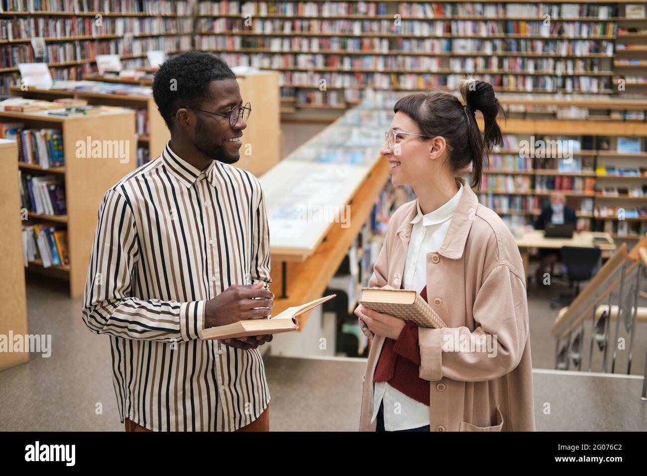 Young happy couple with books talking to each other while standing in ...