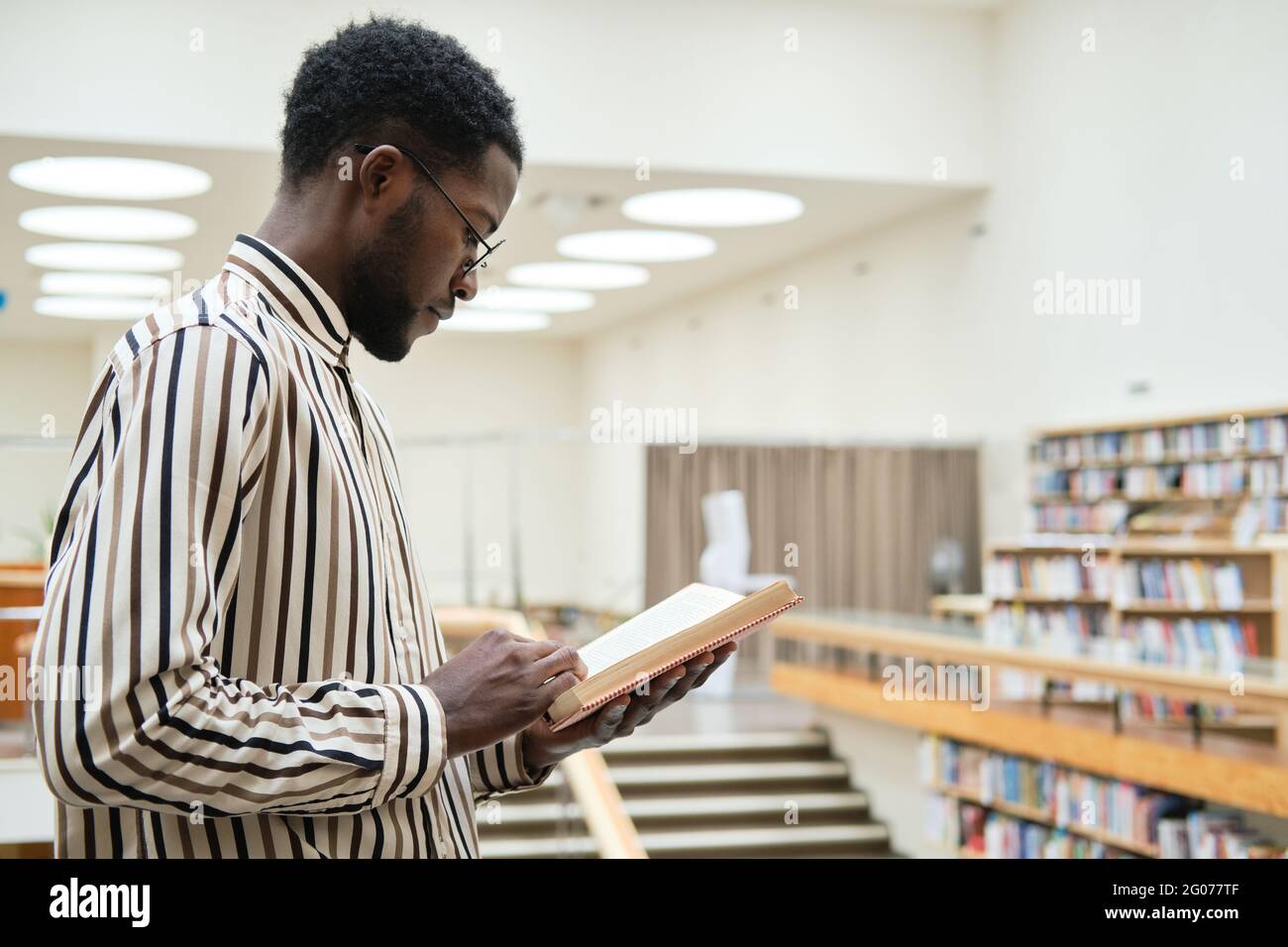 African young man in eyeglasses learning in the library he standing and ...