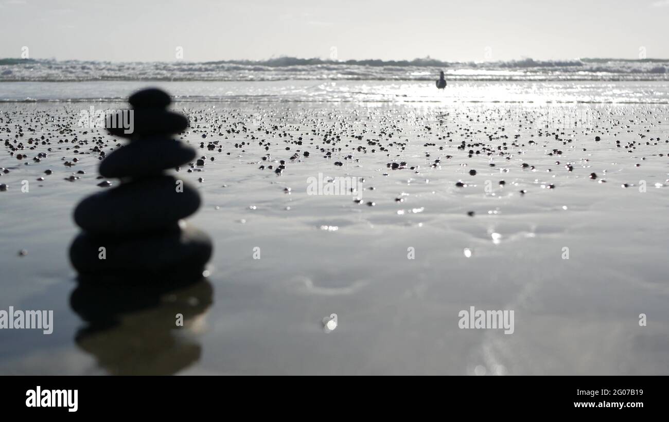 Rock balancing on ocean beach, stones stacking by sea water waves ...
