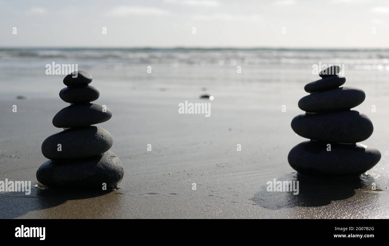 Rock balancing on ocean beach, stones stacking by sea water waves ...