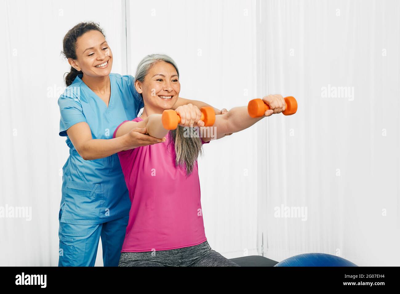 Positive physiotherapist helping her mature woman patient to lift ...