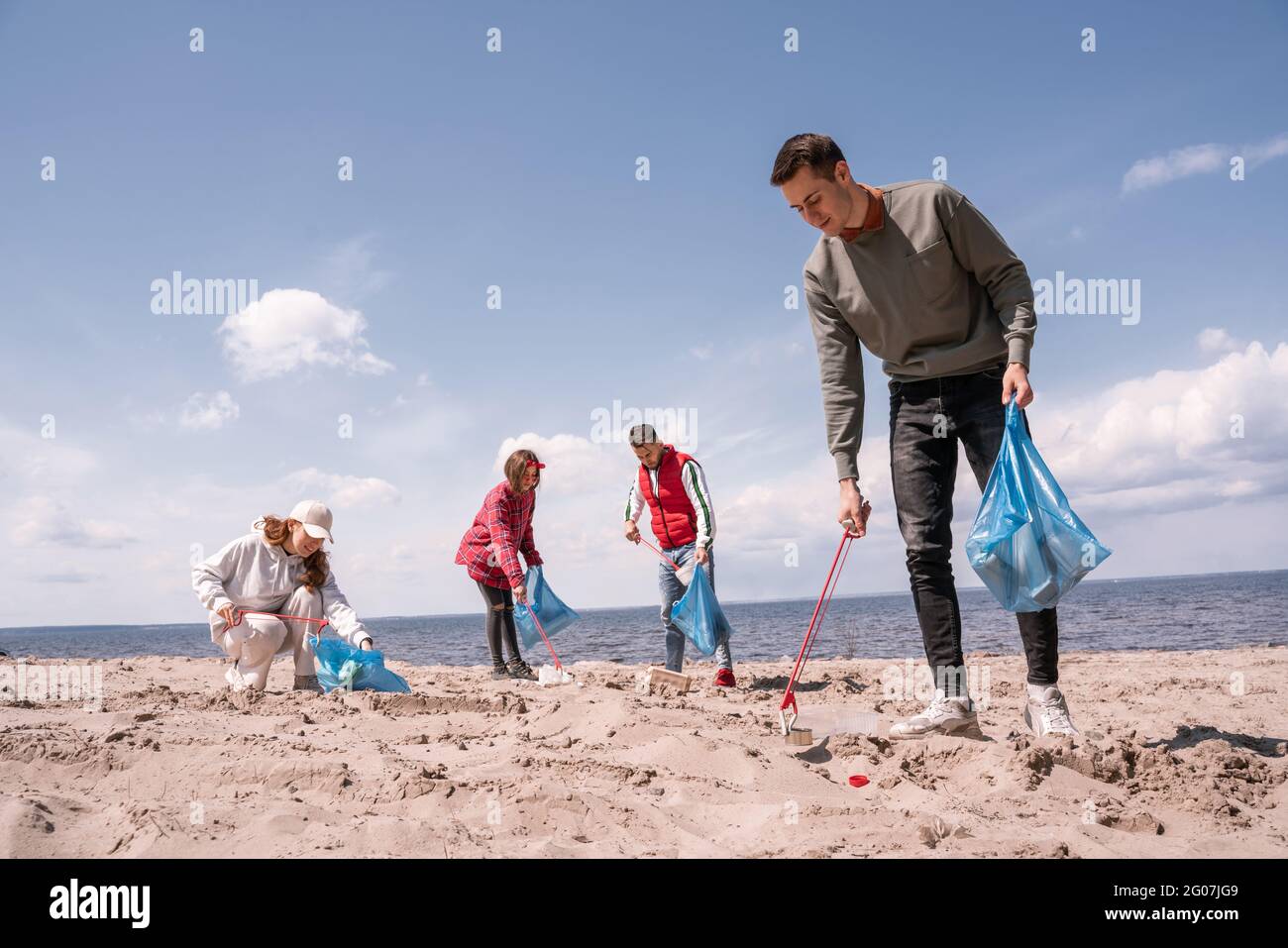 happy man holding trash bag and picking up rubbish on sand near group ...