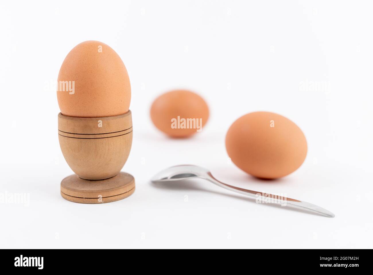 Hen egg in old wooden egg stand with two more eggs and metal spoon ...