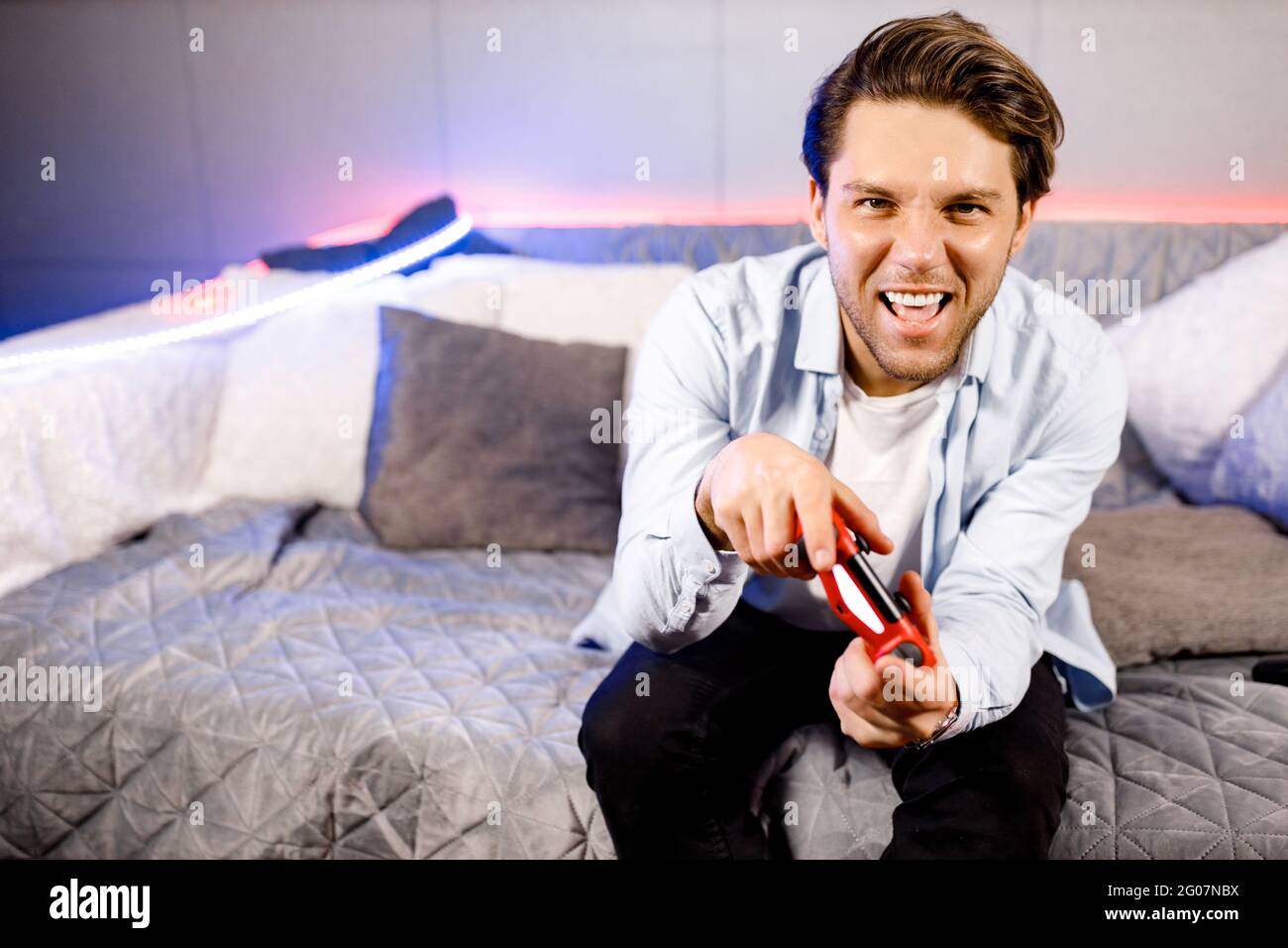 Joyful young Caucasian male playing game at home on console station ...