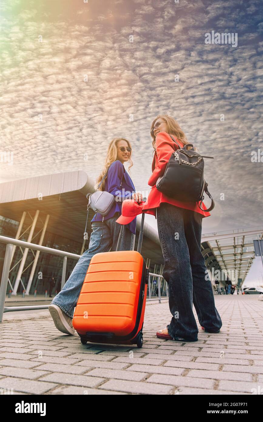 Two happy girls walking near airport, with luggage. Air travel, summer ...