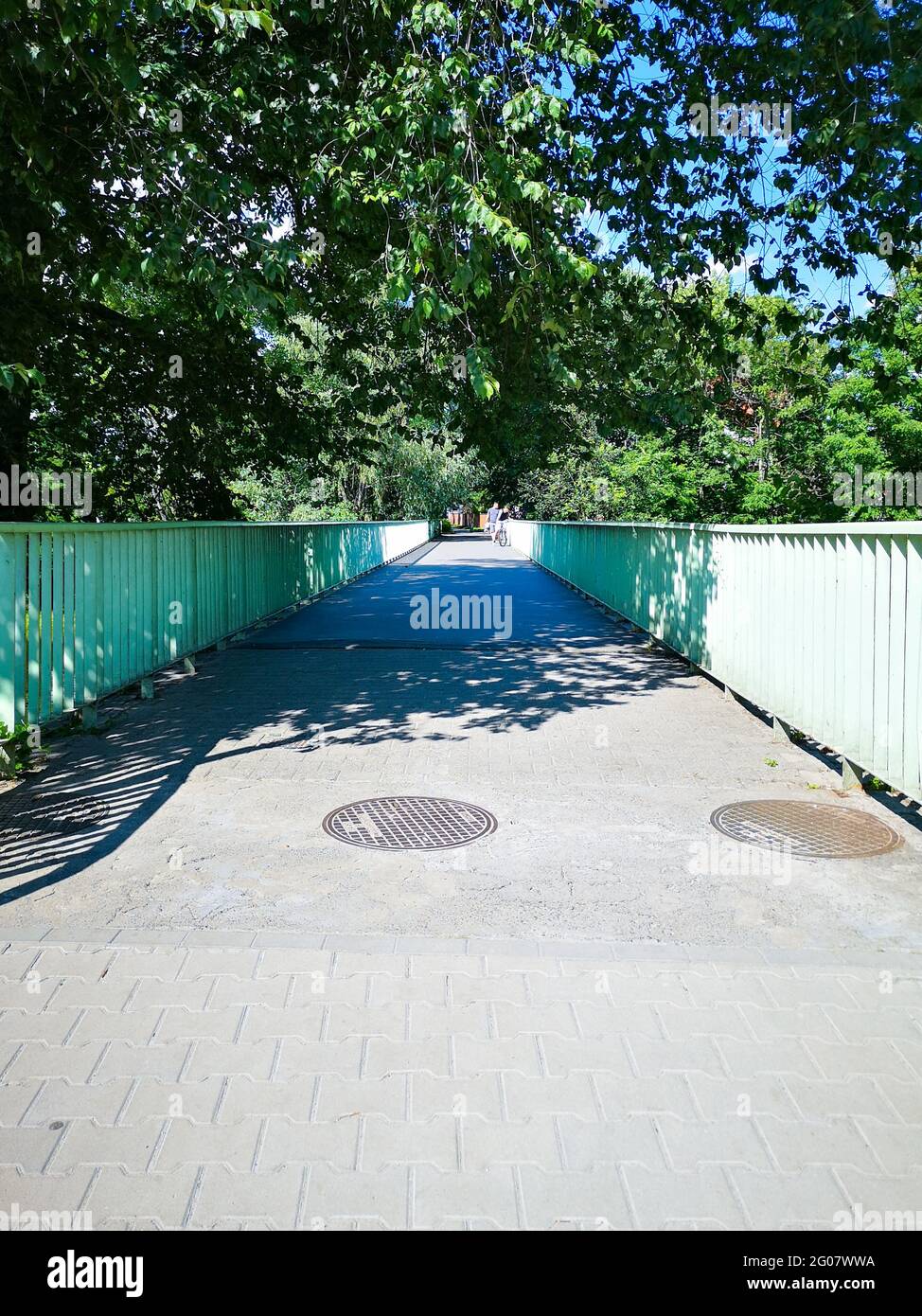 Long narrow concrete bridge with green metal railings on both sides ...