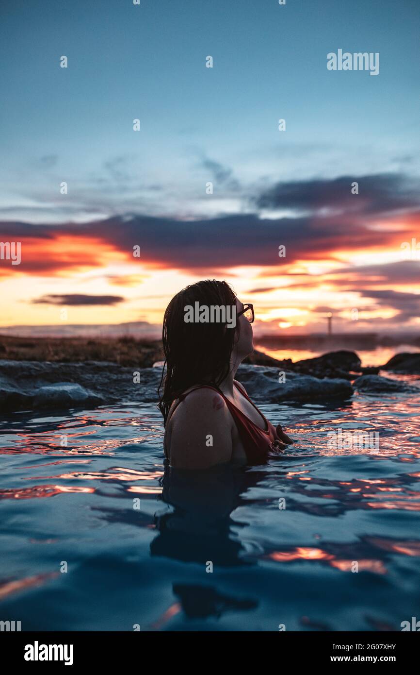 Side view of young Woman in swimsuit posing in blue water between rocks ...