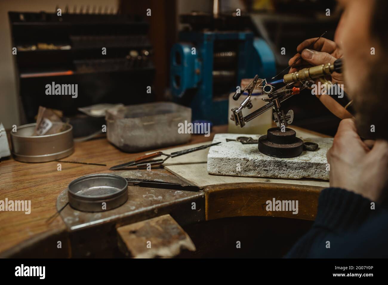 Anonymous goldsmith using blowtorch to heat tiny metal ornament while ...