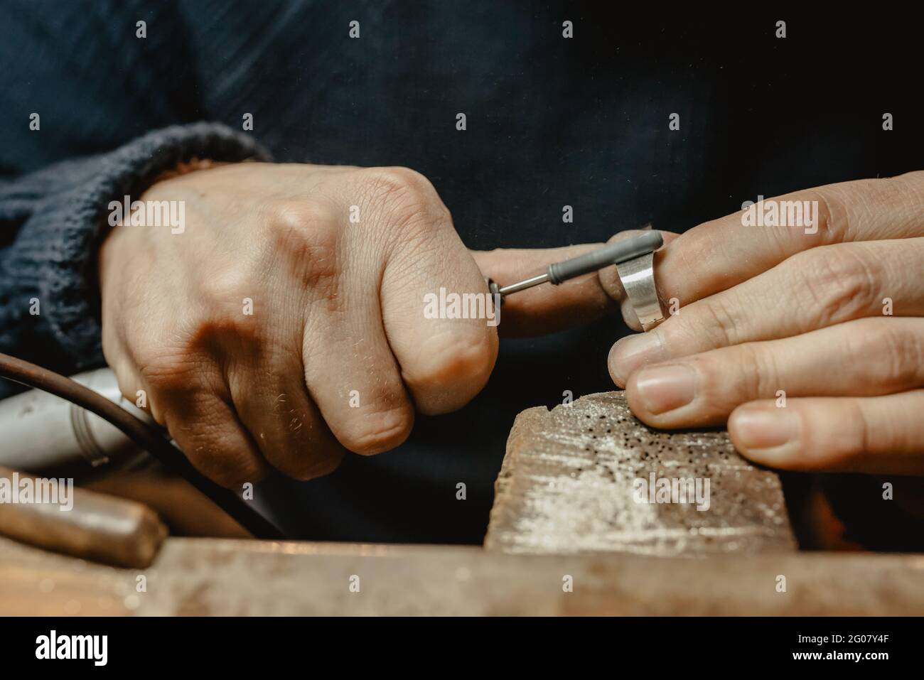 Hands of anonymous male goldsmith using manual tool to shape metal ring ...