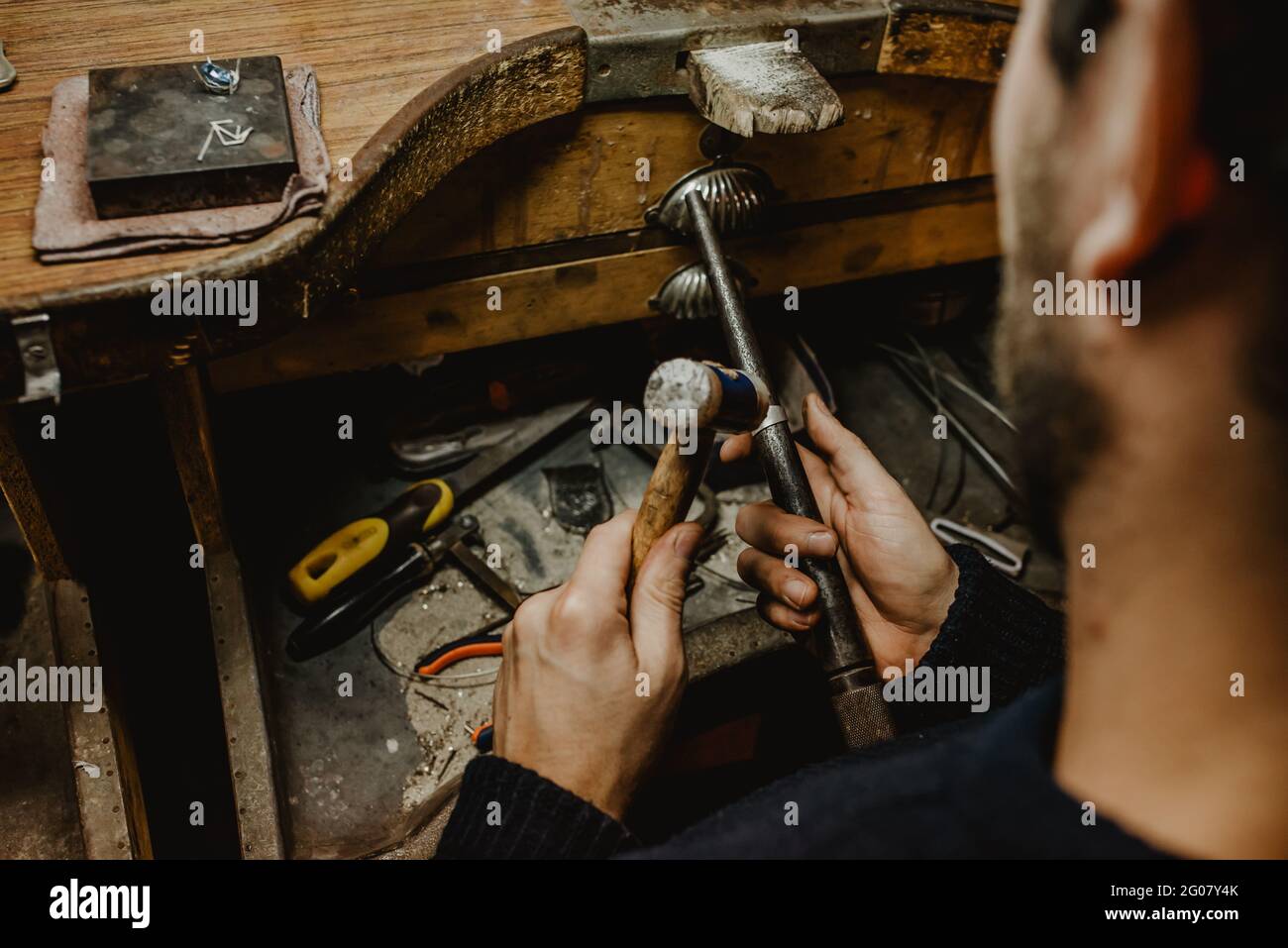 Anonymous goldsmith hammering and expanding ring blank on metal stick ...