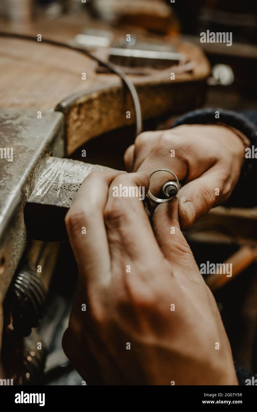 Hands of anonymous male goldsmith using manual tool to shape metal ring ...