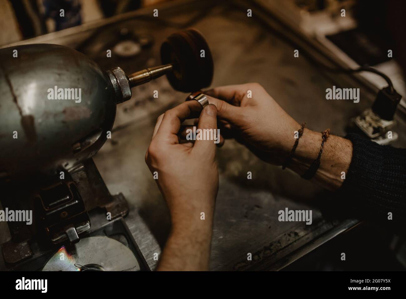 Hands of anonymous male goldsmith using manual tool to shape metal ring ...