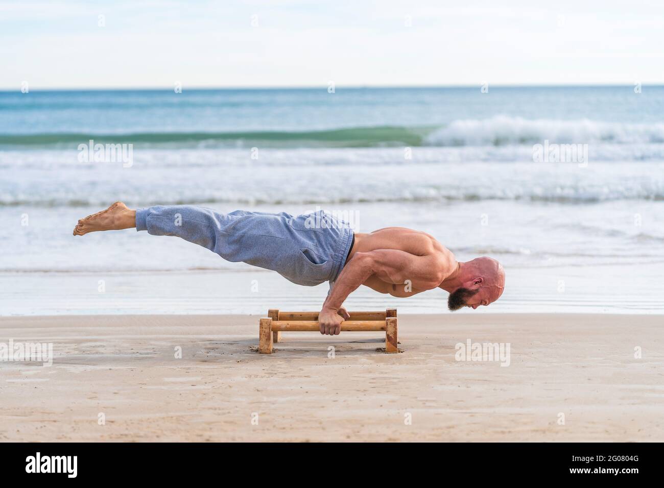 Side view of bald strong athlete doing parallel handstand with bars ...