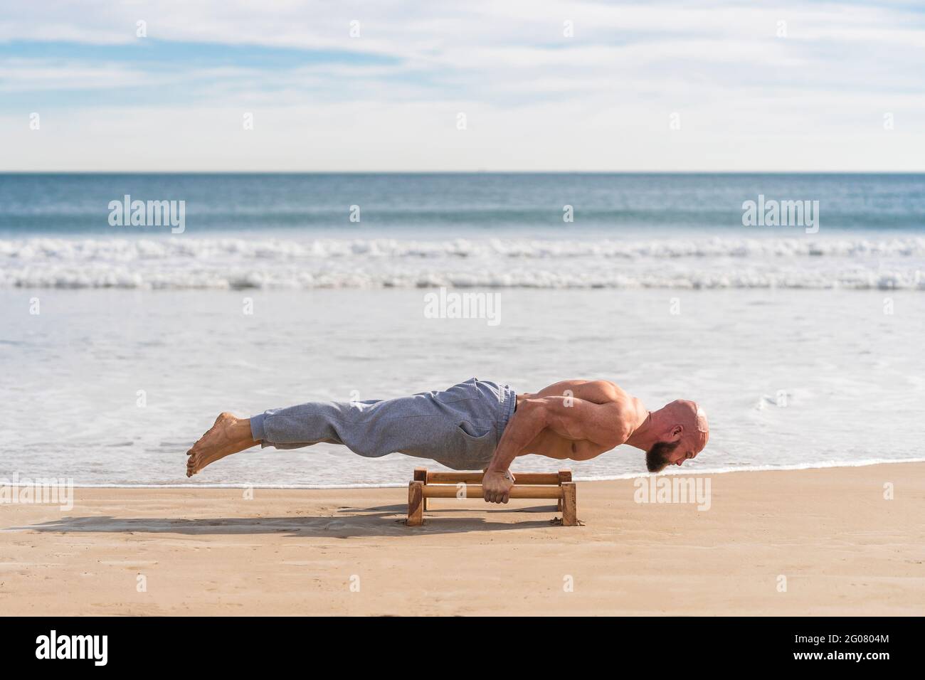 Side view of bald strong athlete doing parallel handstand with bars ...