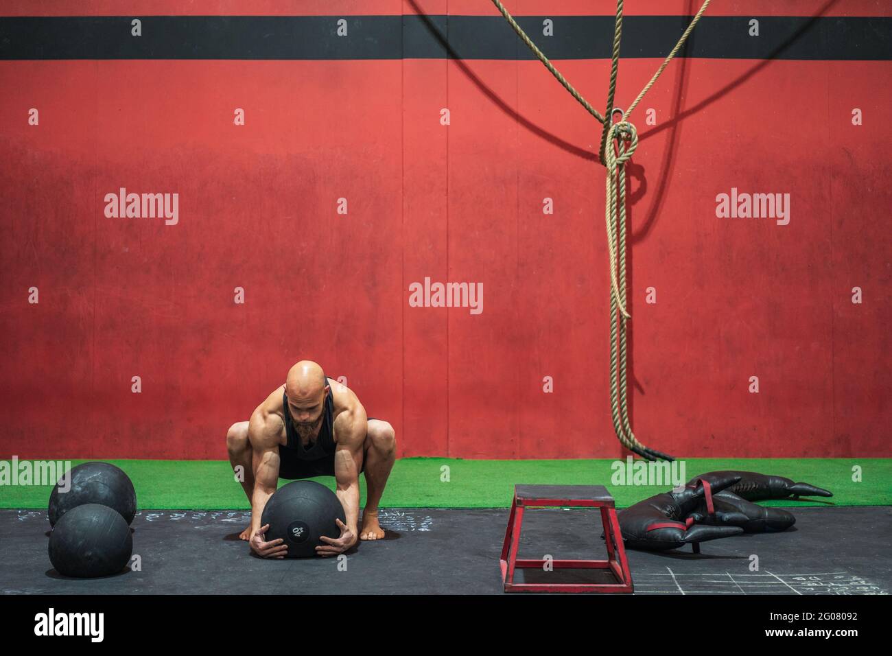 Strong male athlete lifting heavy ball from the floor while exercising ...