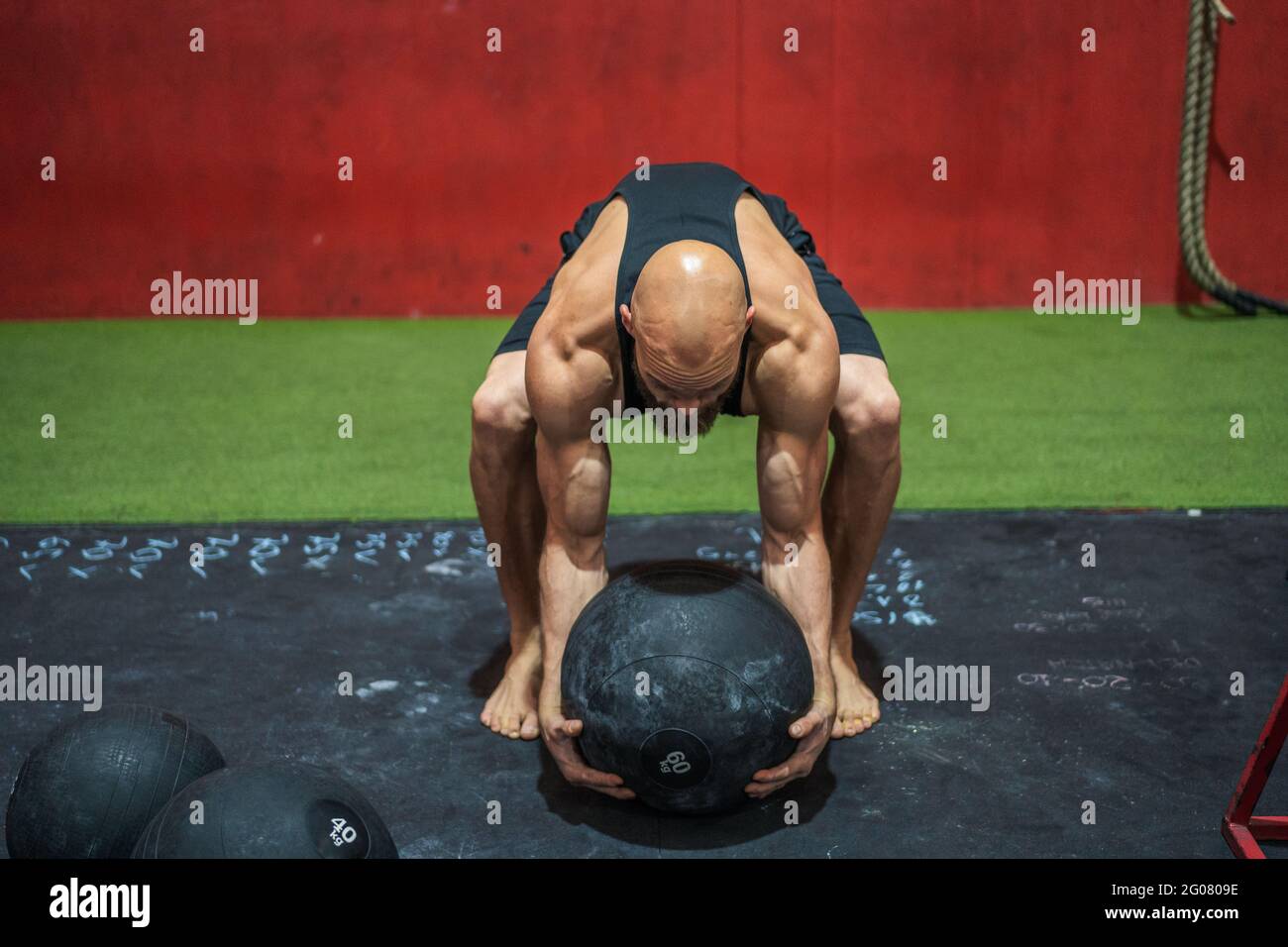 Strong male athlete lifting heavy ball from the floor while exercising ...