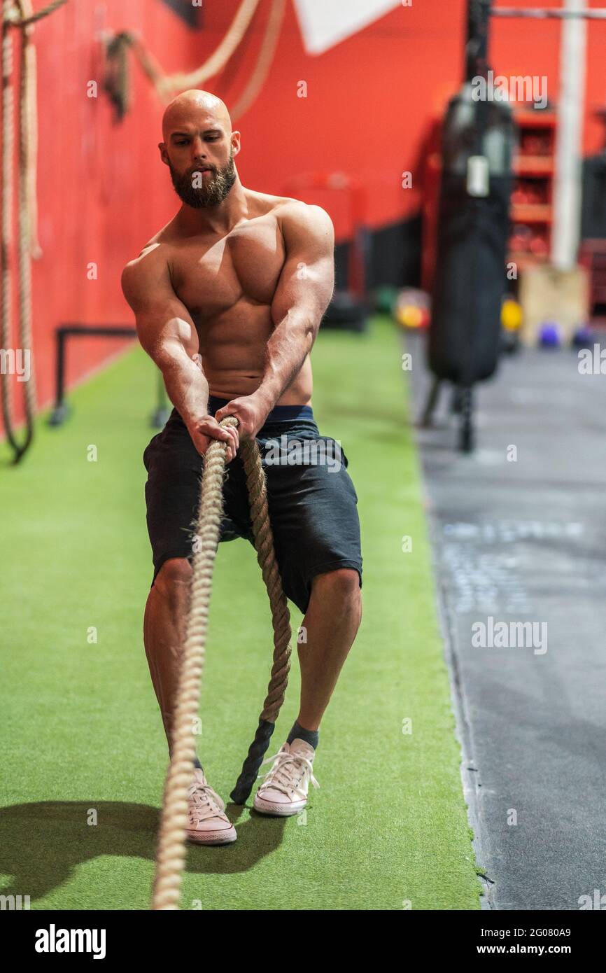 Strong sportsman pulling rope with heavy weights during intense workout ...