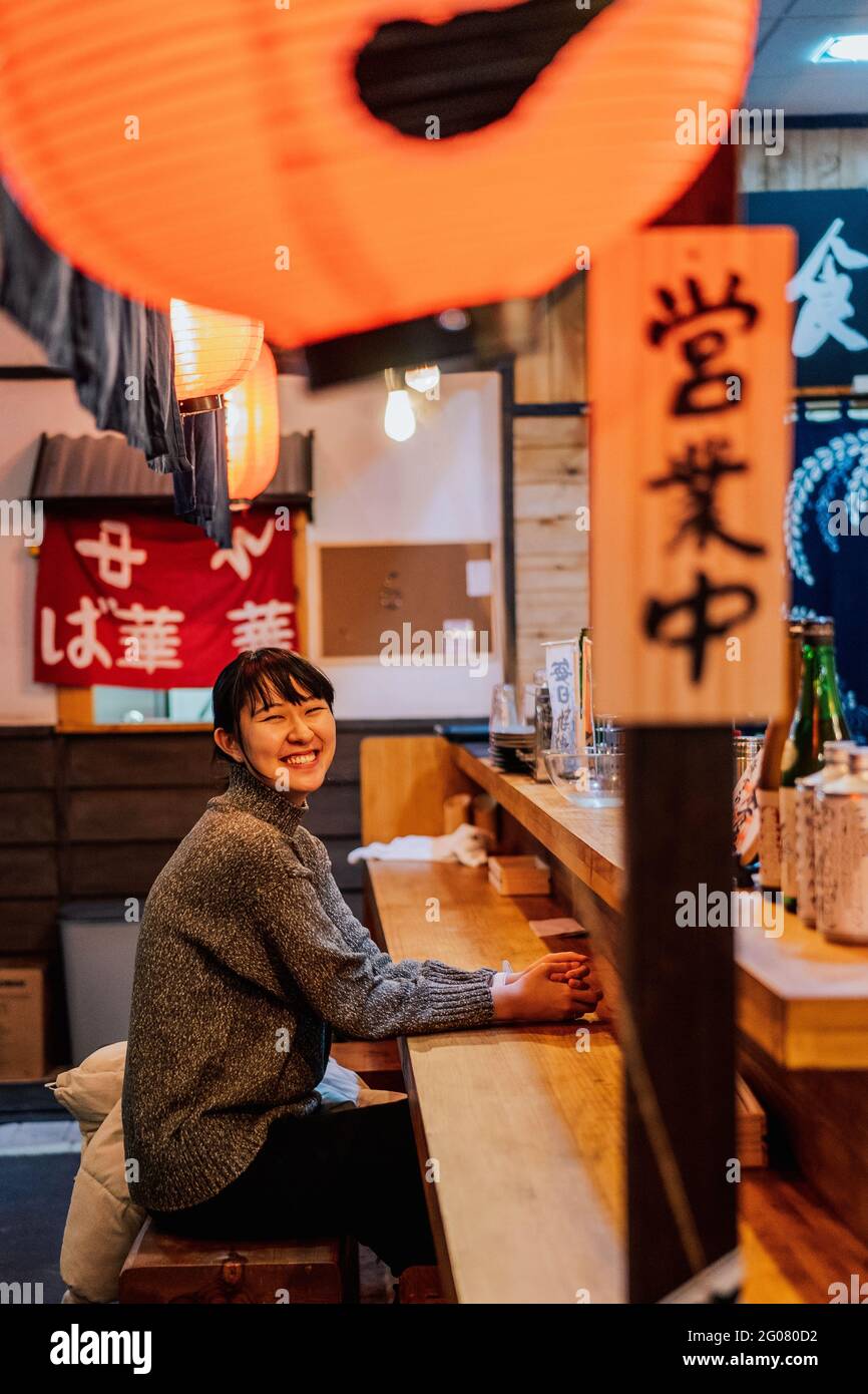 Asian Woman in casual wear sitting at wooden counter while waiting for ...