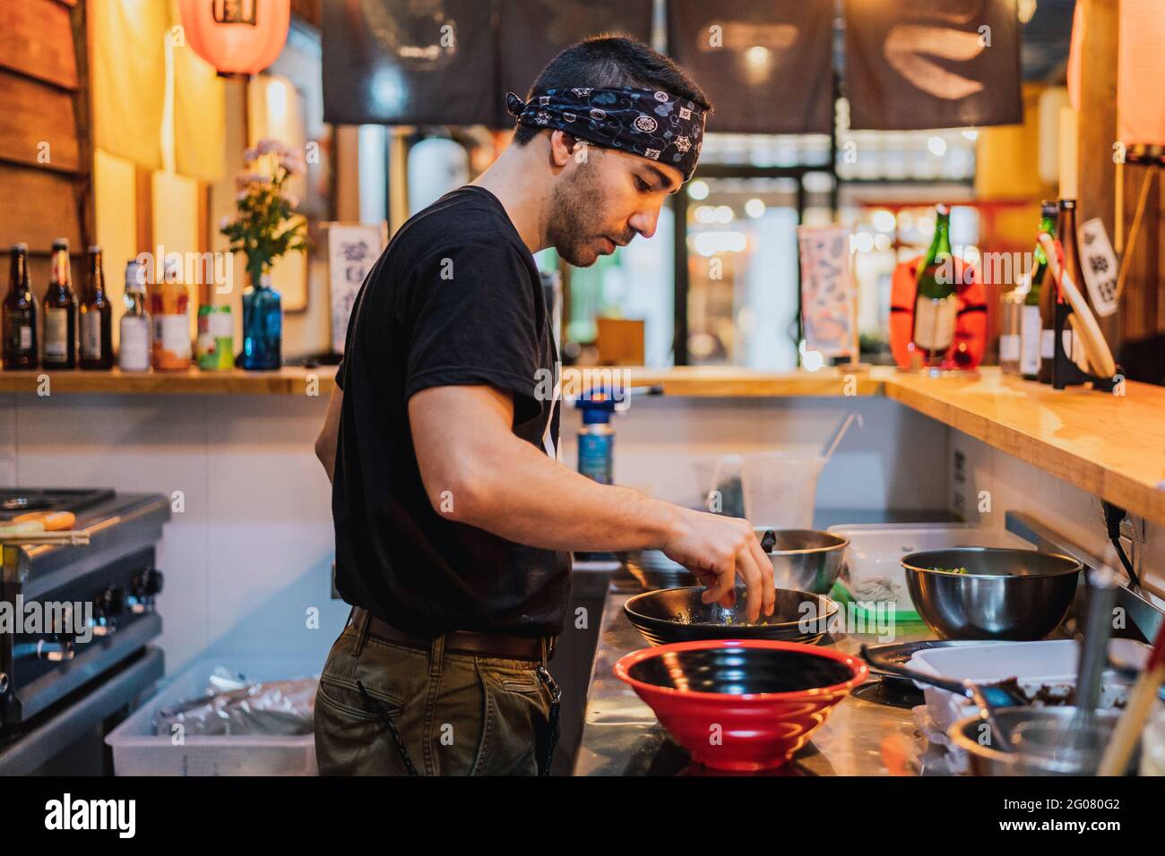 Side view of man in bandana standing at counter and cooking ramen in ...