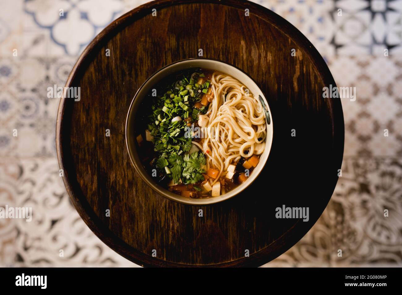 From above ceramic bowl with Chinese ramen meal on circle wooden tray ...