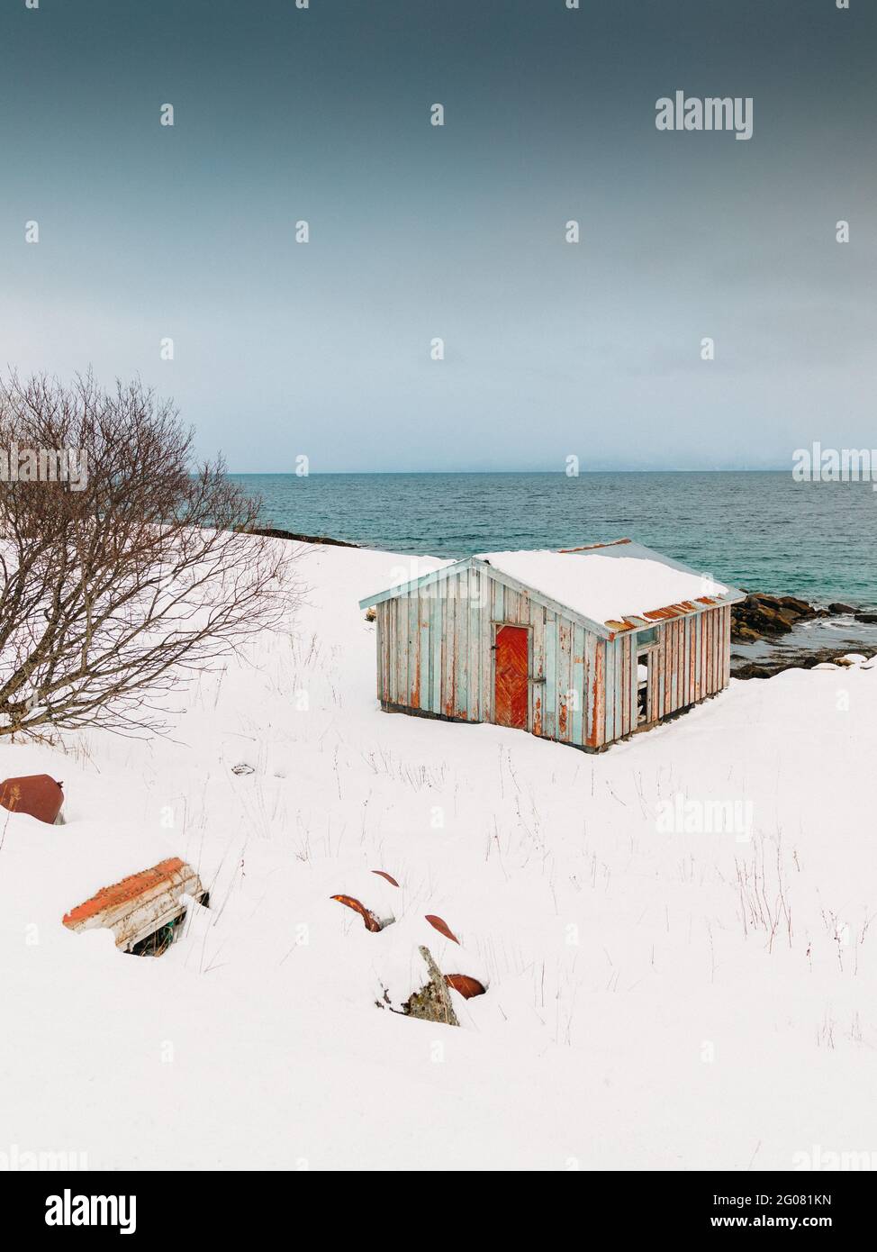 Weathered wooden shack located on white snowy coast of sea against ...