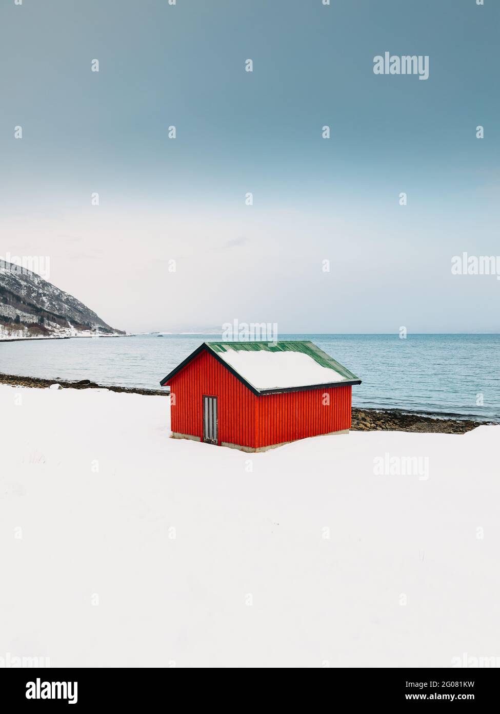 Red shack located on white snowy coast of sea against cloudless blue ...
