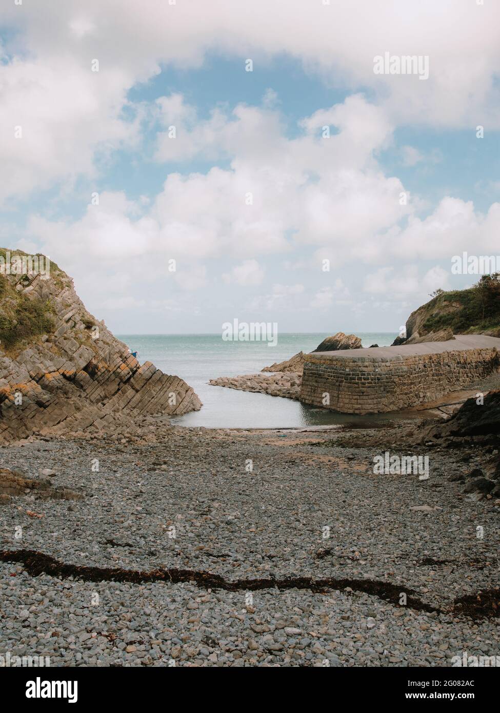Rough stony coast of calm sea and brick pier with road on cloudy day in ...