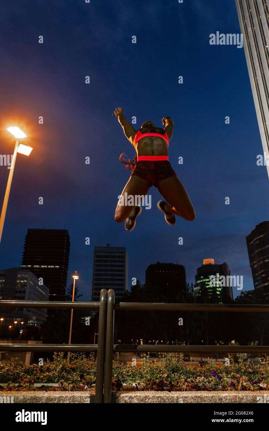 From below African American athletic Woman jumping on street at night ...