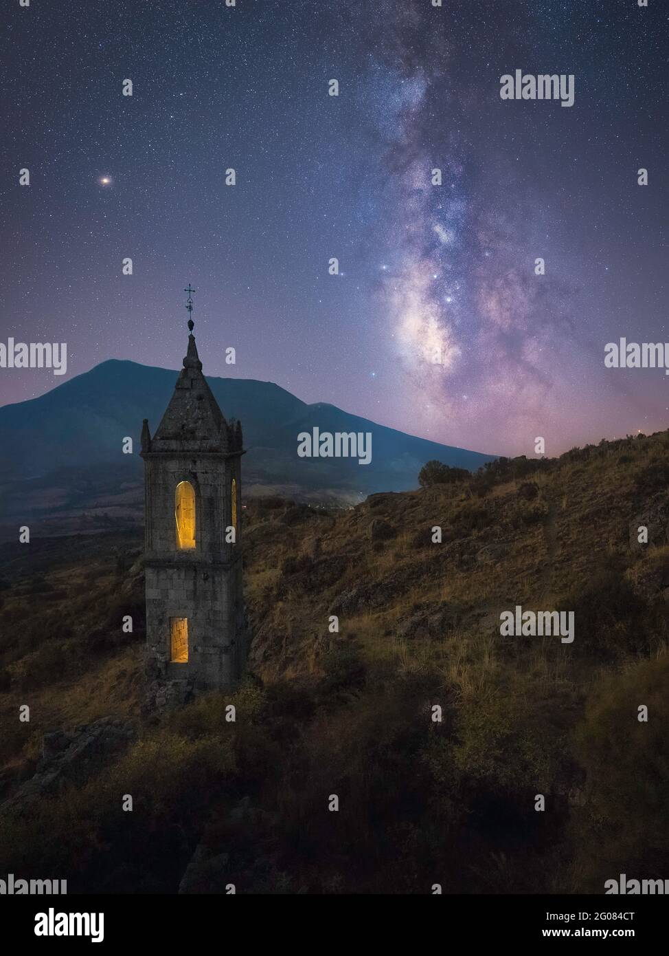 Beautiful night sky with bright stars over hilly terrain and aged tower ...