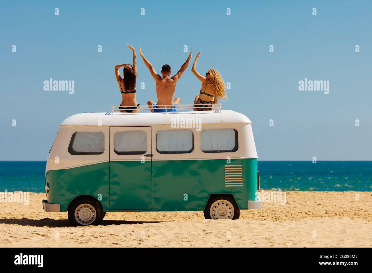 Three tourist sitting on roof of hippie car on sandy beach Stock Photo ...