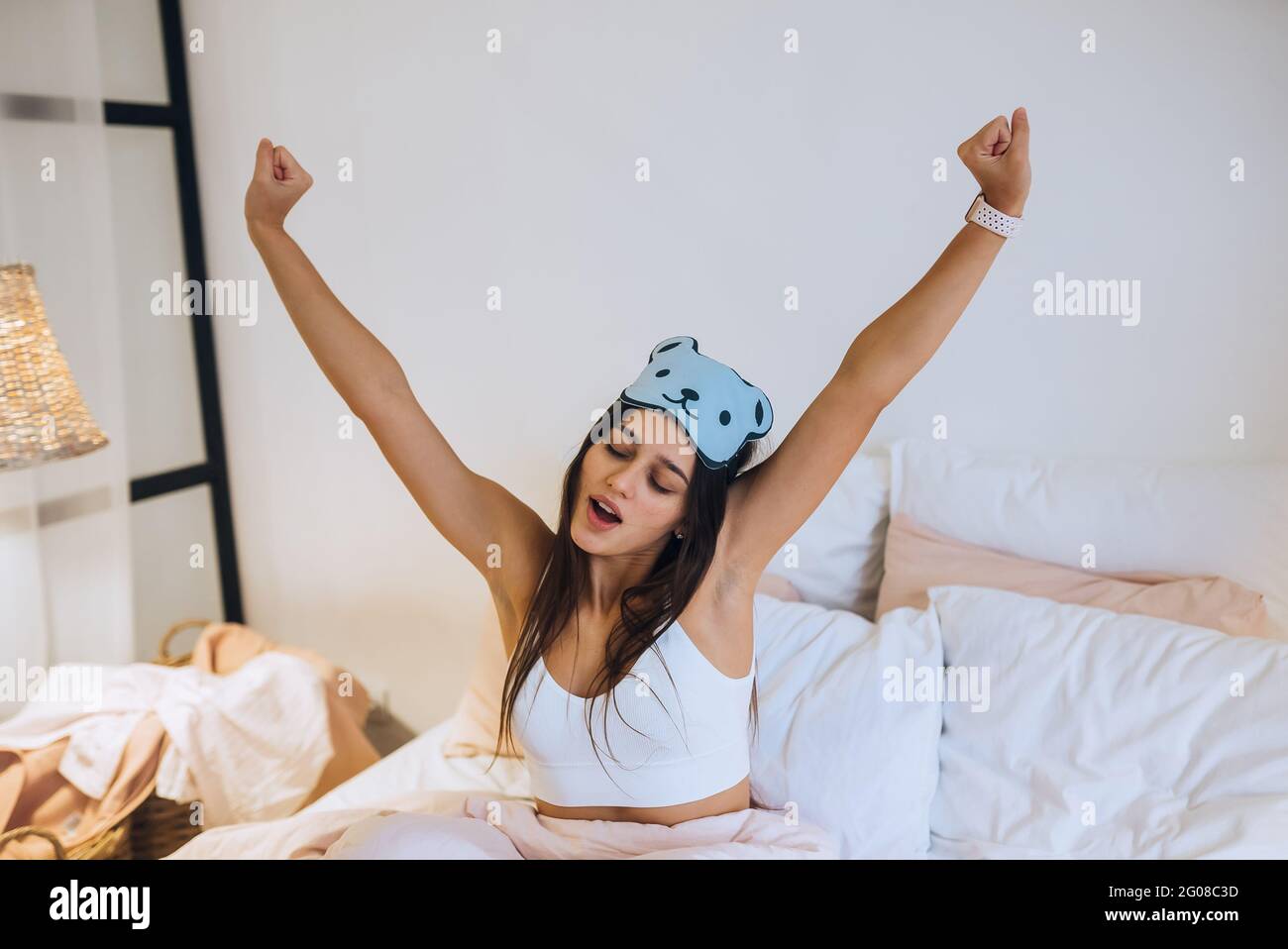Sleepy woman waking up while sitting in bed isolated on white ...
