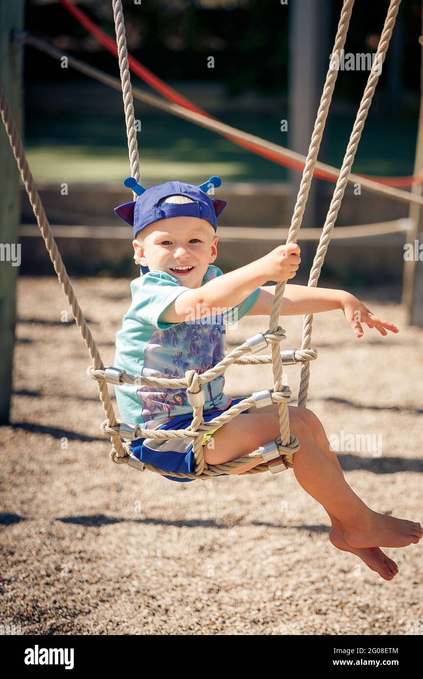 A handsome boy in a blue cap rides on a swing Stock Photo - Alamy