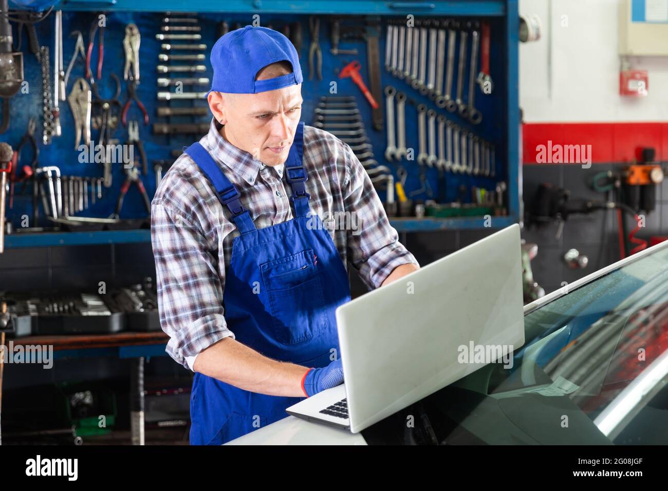 Male mechanic using laptop while repairing car in service Stock Photo ...