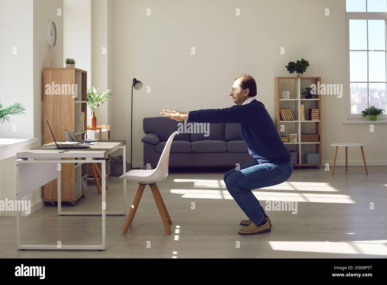 Mature businessman doing squat exercise front of laptop computer in ...