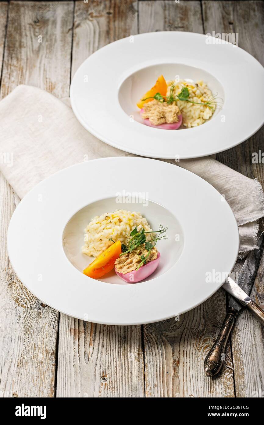 Two servings of seafood risotto in white plates. Egg with smoked ...