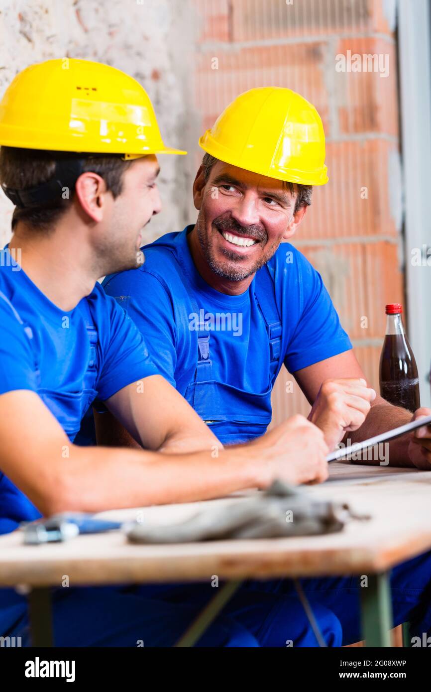 Builders having break on construction site sitting down drinking ...