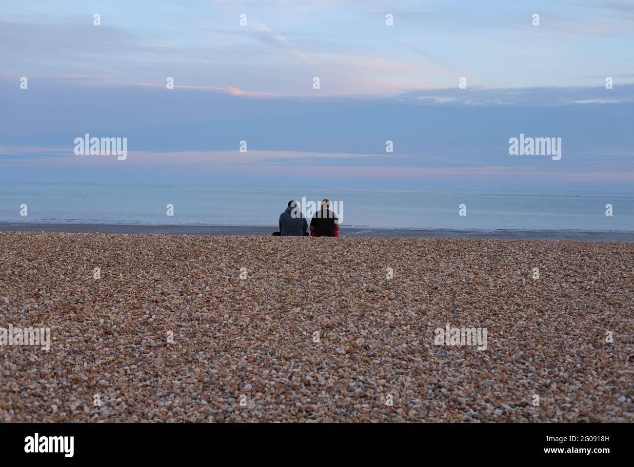 Two people seen sitting on the shingle beach on the south coast of the ...