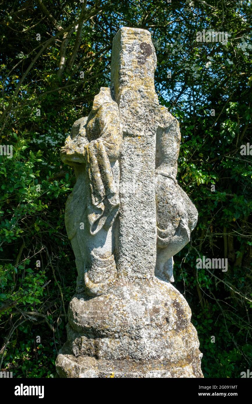 A heavily damaged statue of two figures, one Christ a cross on a stone ...