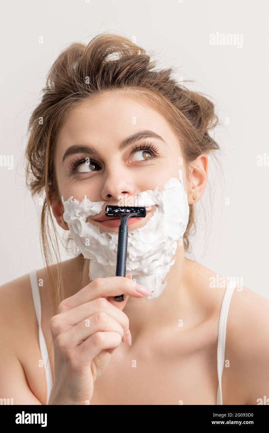 Beautiful young caucasian smiling woman shaving her face with razor ...