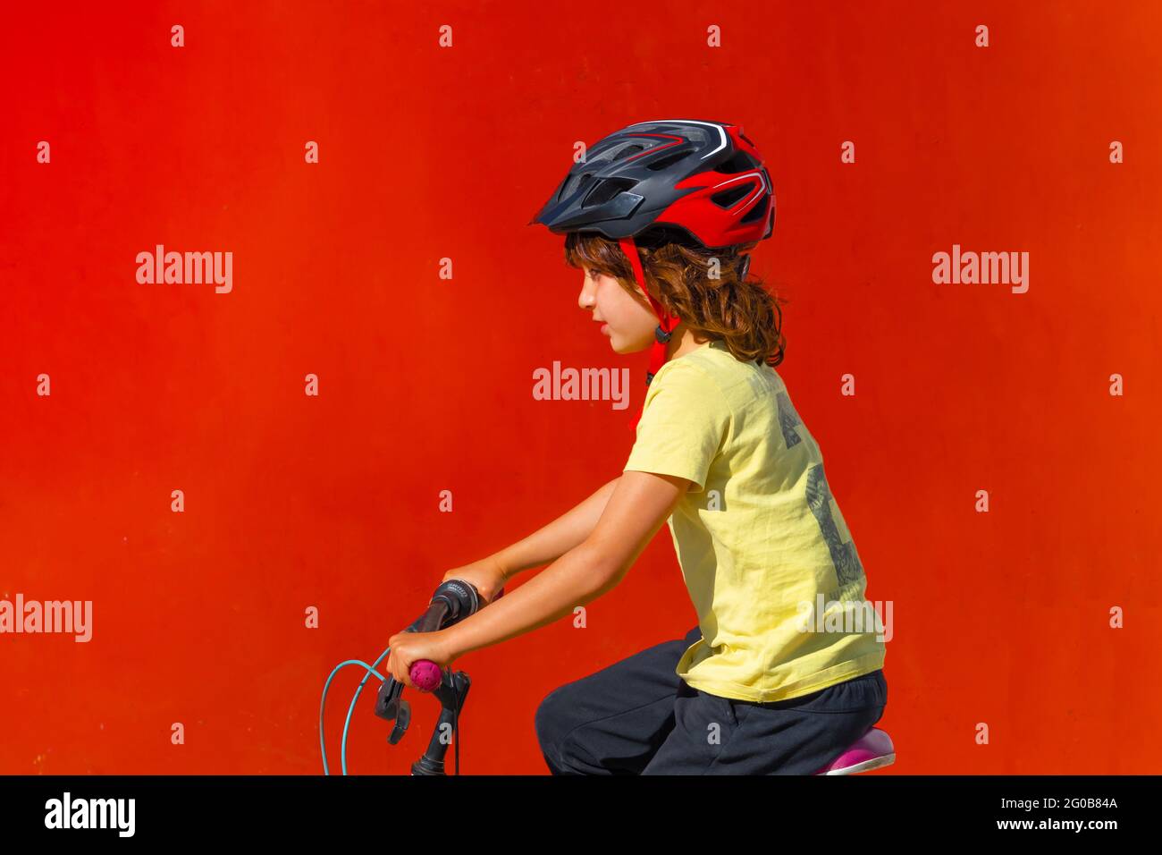 little boy in profile on red background riding bike with safety helmet ...